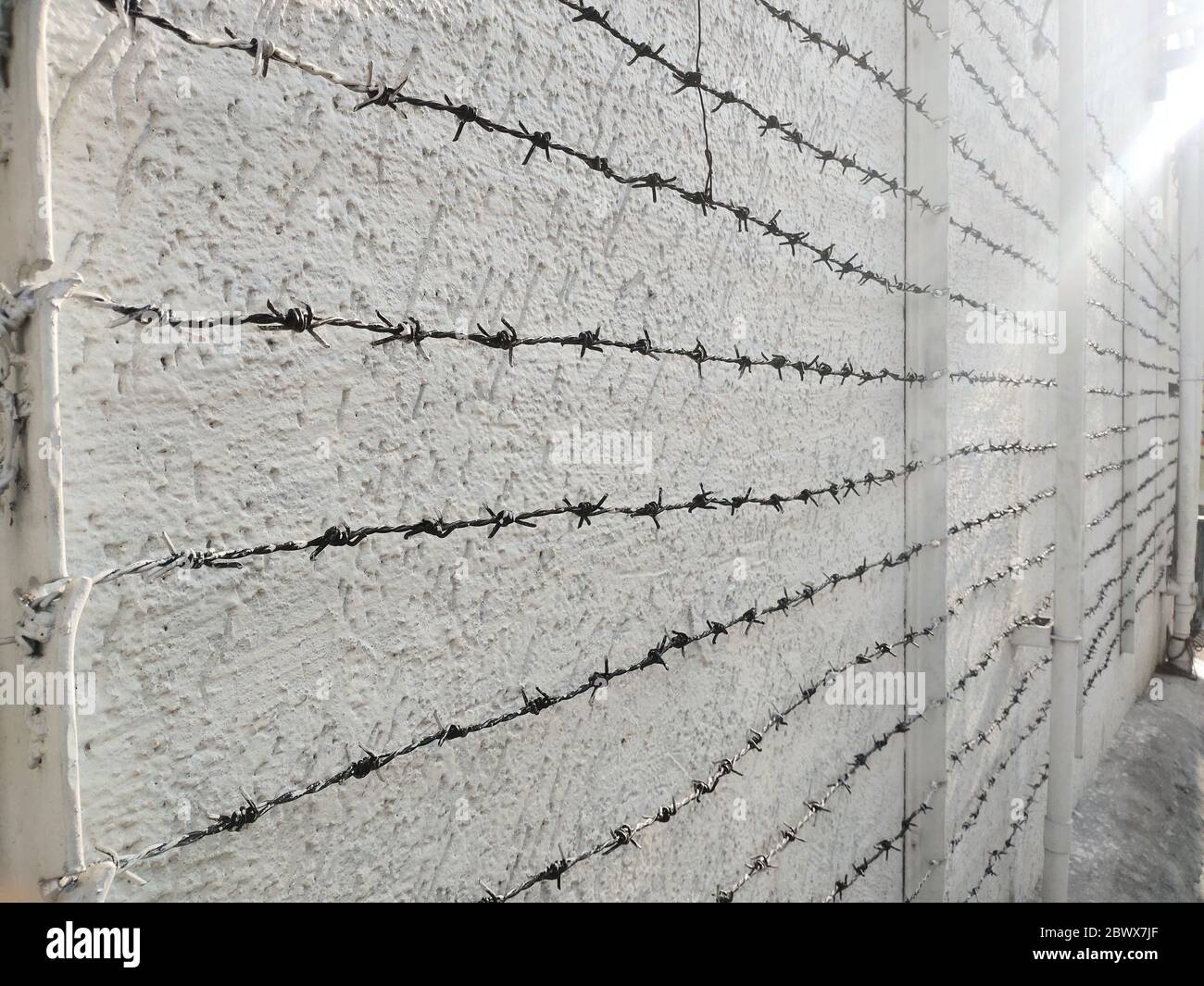 Sharp rusty steel barbed wire covered on the white building wall. Long ...