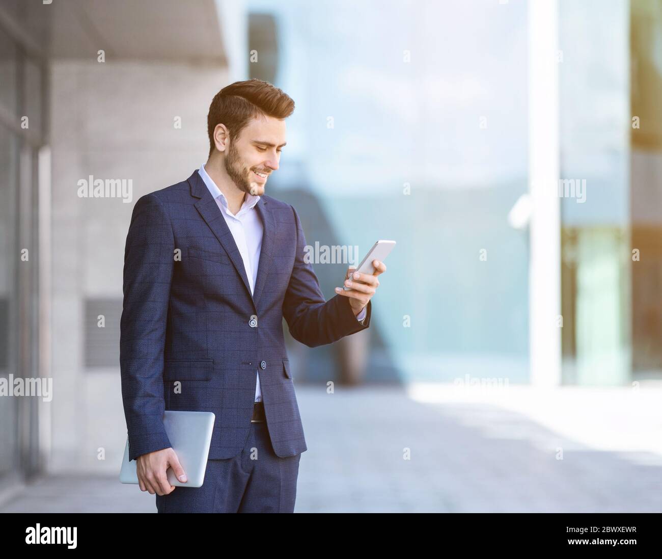 Smiling broker in formal suit with cellphone and tablet at downtown ...