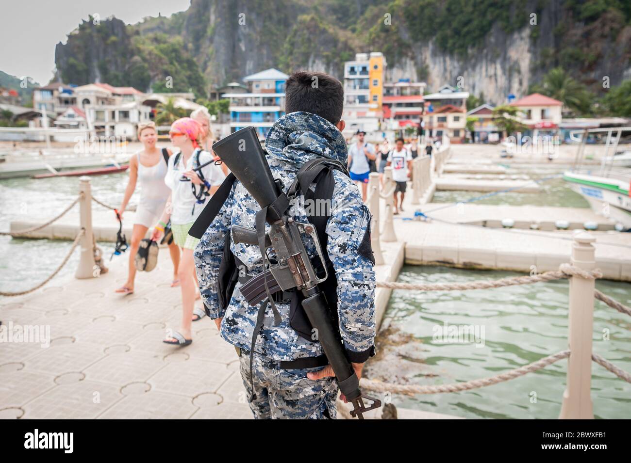 An armed Filipino coast guard watches tourists board day boats heading ...