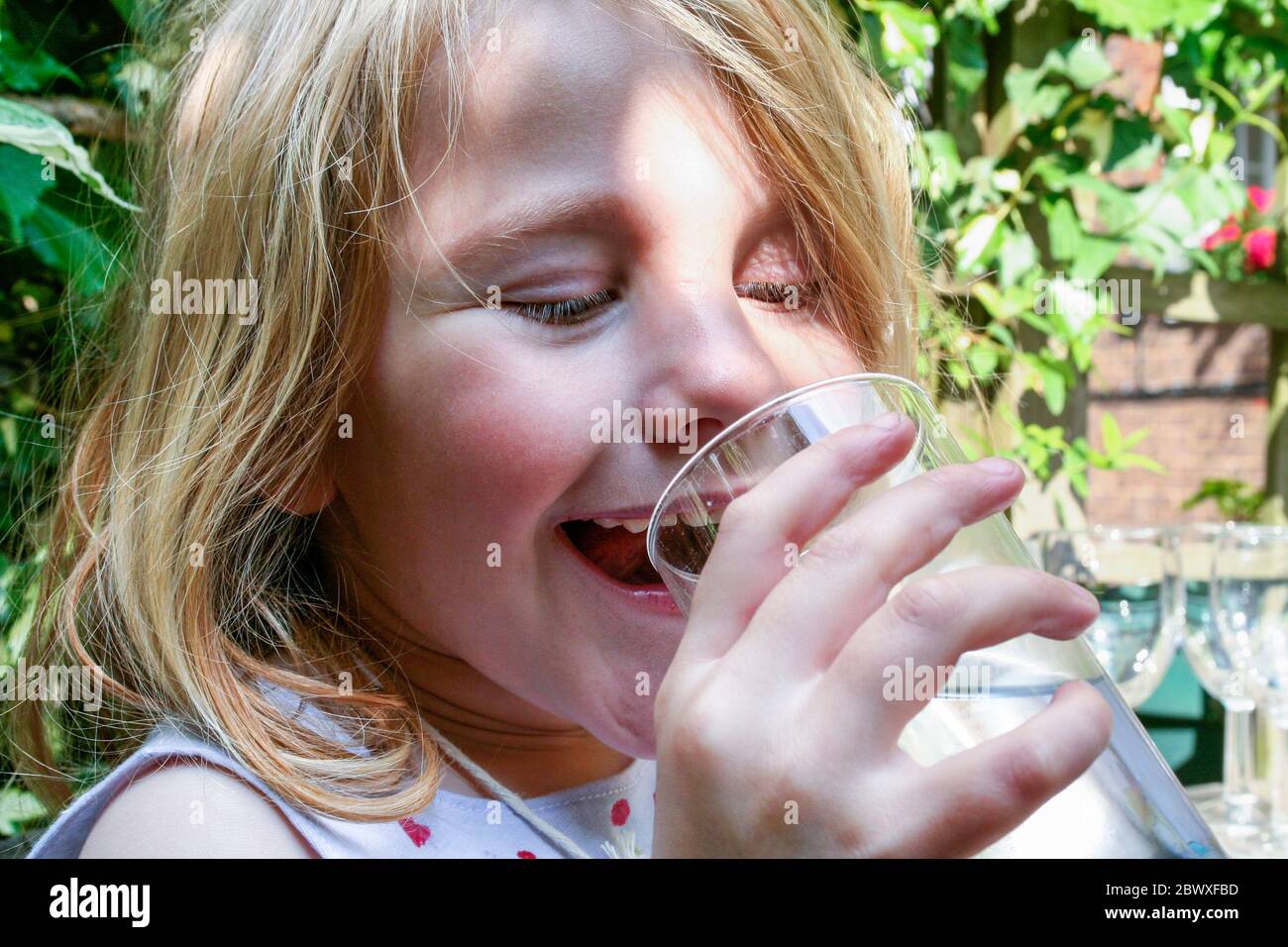 A seven year-old girl laughing while drinking water from a glass ...