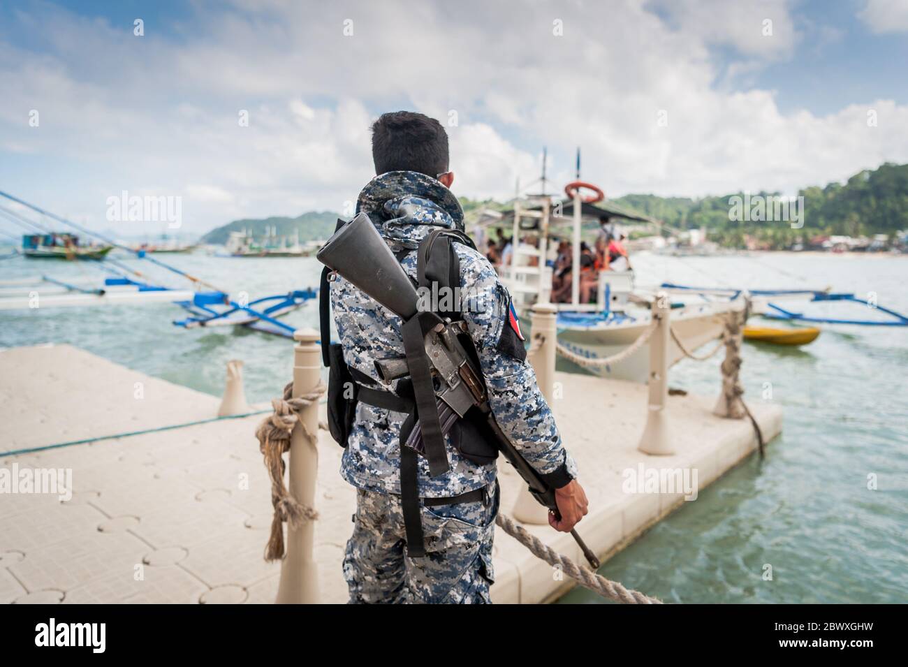 An armed Filipino coast guard watches tourists board day boats heading ...