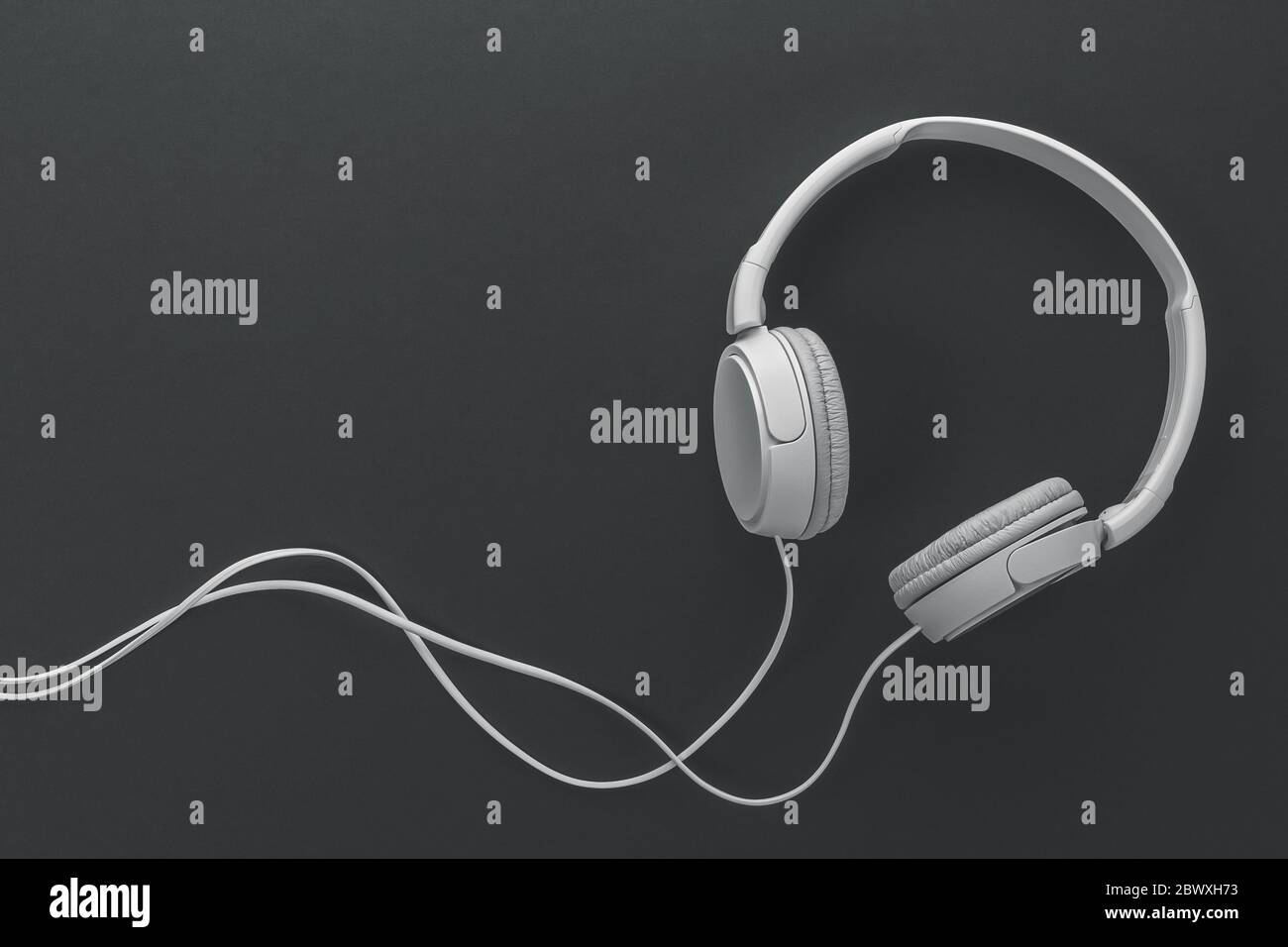 Flat lay modern white headphones with a curved wire on a black ...