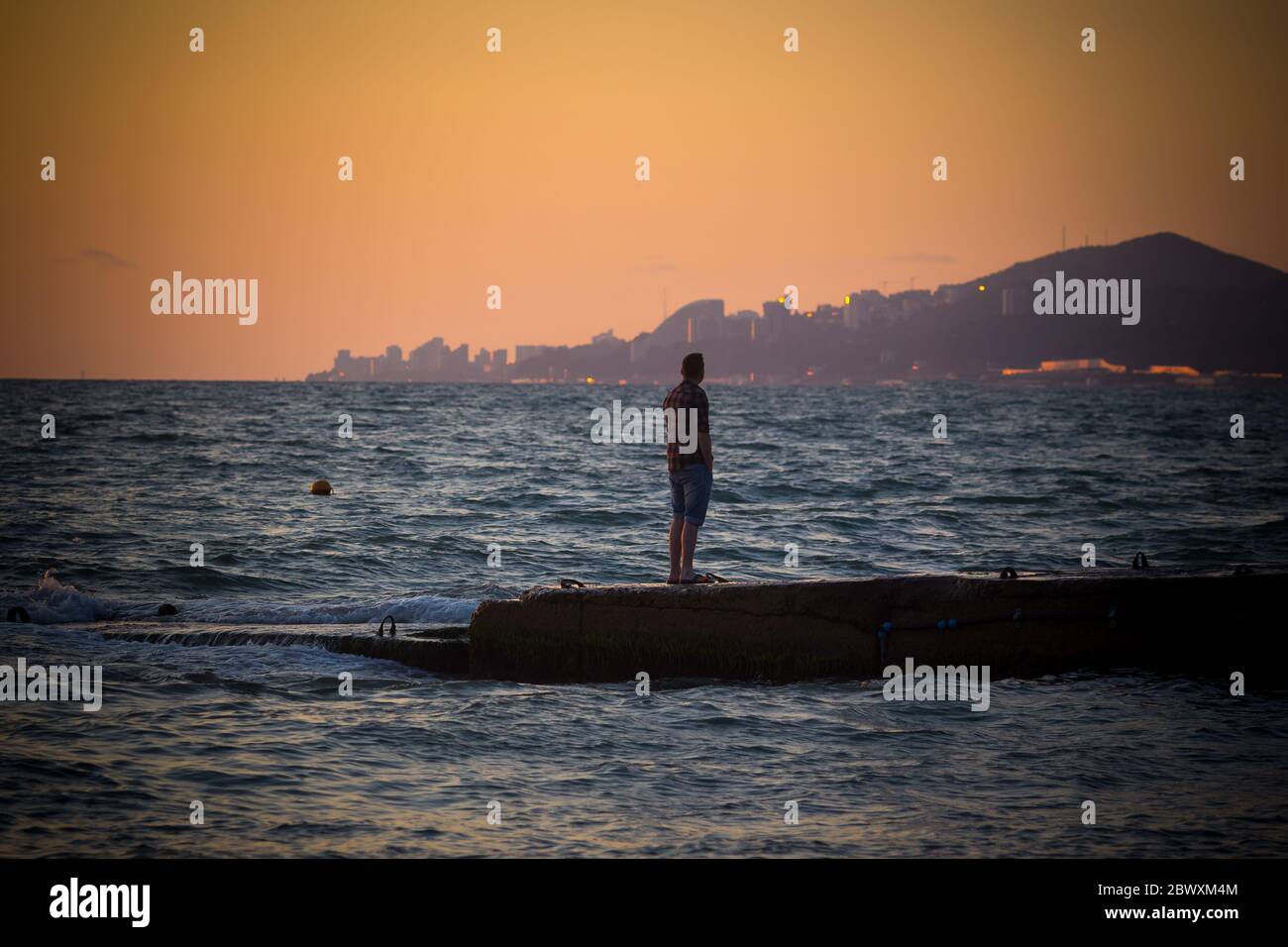 Man watching the cityscape fom the water dusk scene Stock Photo - Alamy