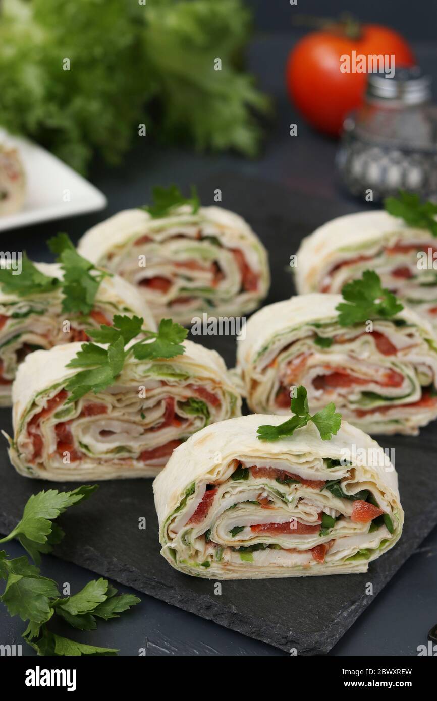 Pita roll with smoked chicken, tomatoes and cheese located on dark ...