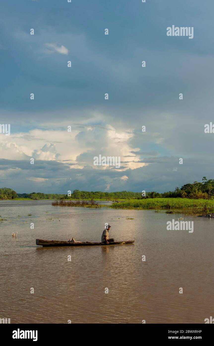 A man in a canoe is fishing on the Amazon River in the Peruvian Amazon ...