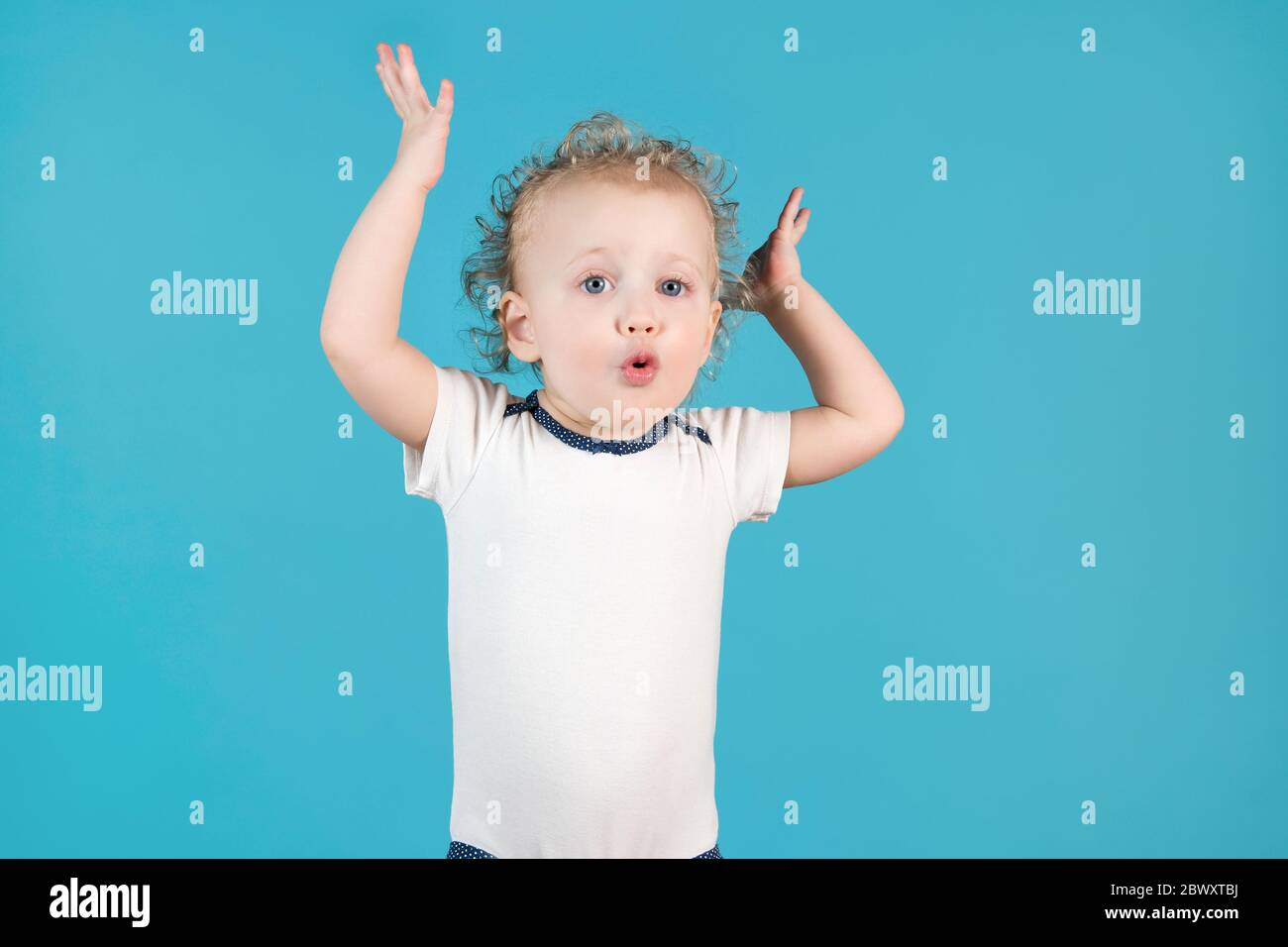 Funny curly baby girl of two years makes a surprised face and raises ...