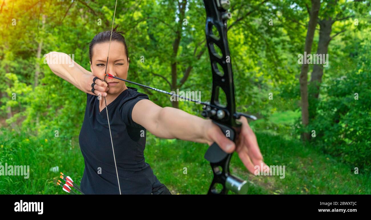 archery, young woman with an arrow in a bow focused on hitting a target ...