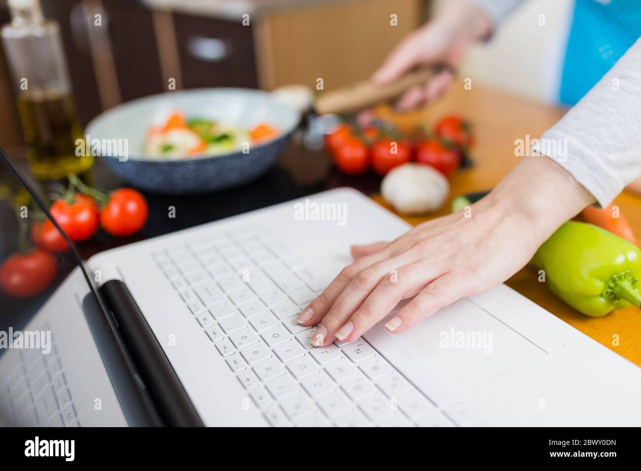 Close up of female hand on laptop keyboard while holding cooking pan ...