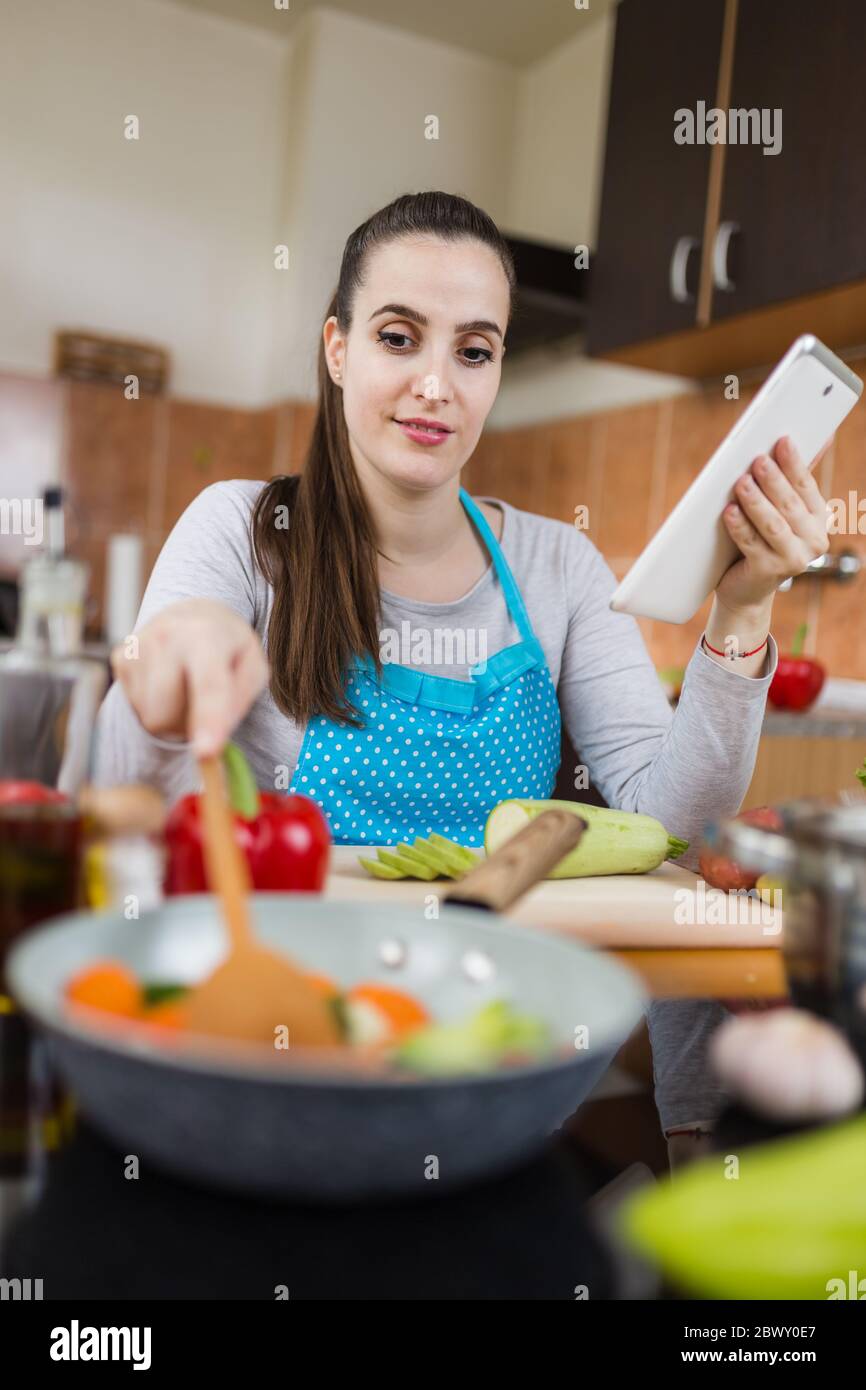 Young housewife learning to cook by watching online video recipe ...