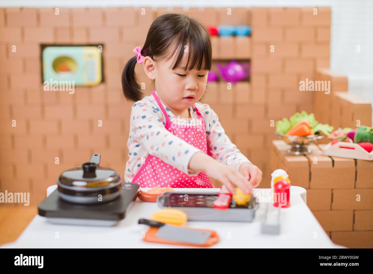 toddler girl pretend play food preparing role against cardboard blocks ...