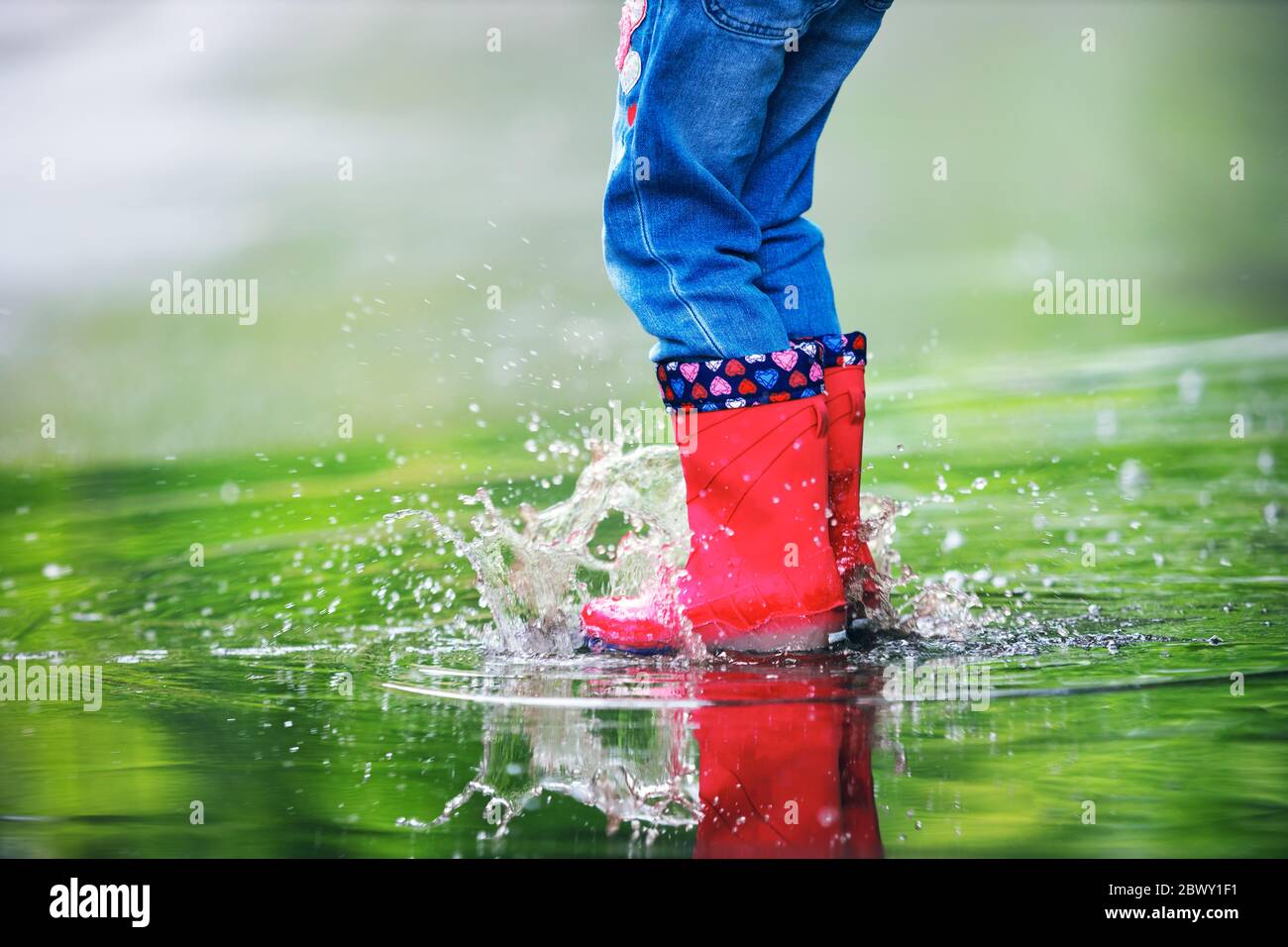 Happy child girl with red rubber boots jumping in puddle at the spring ...