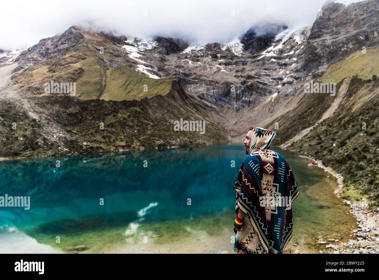 Man standing by a beautiful blue lake in the middle of the mountains in ...