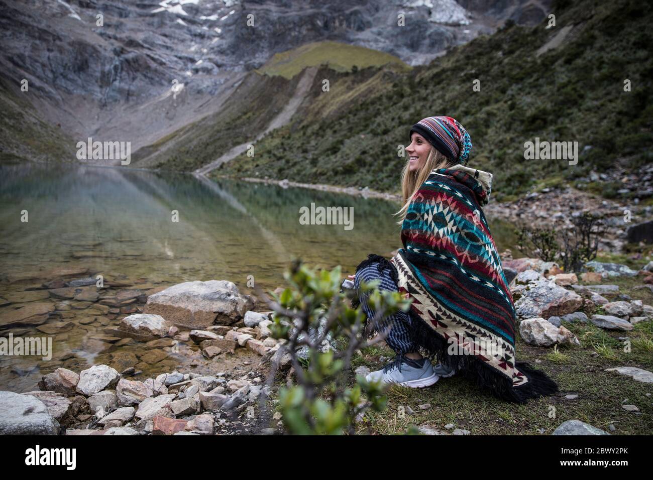 Beautiful blonde woman sitting by a blue lake in the middle of the ...