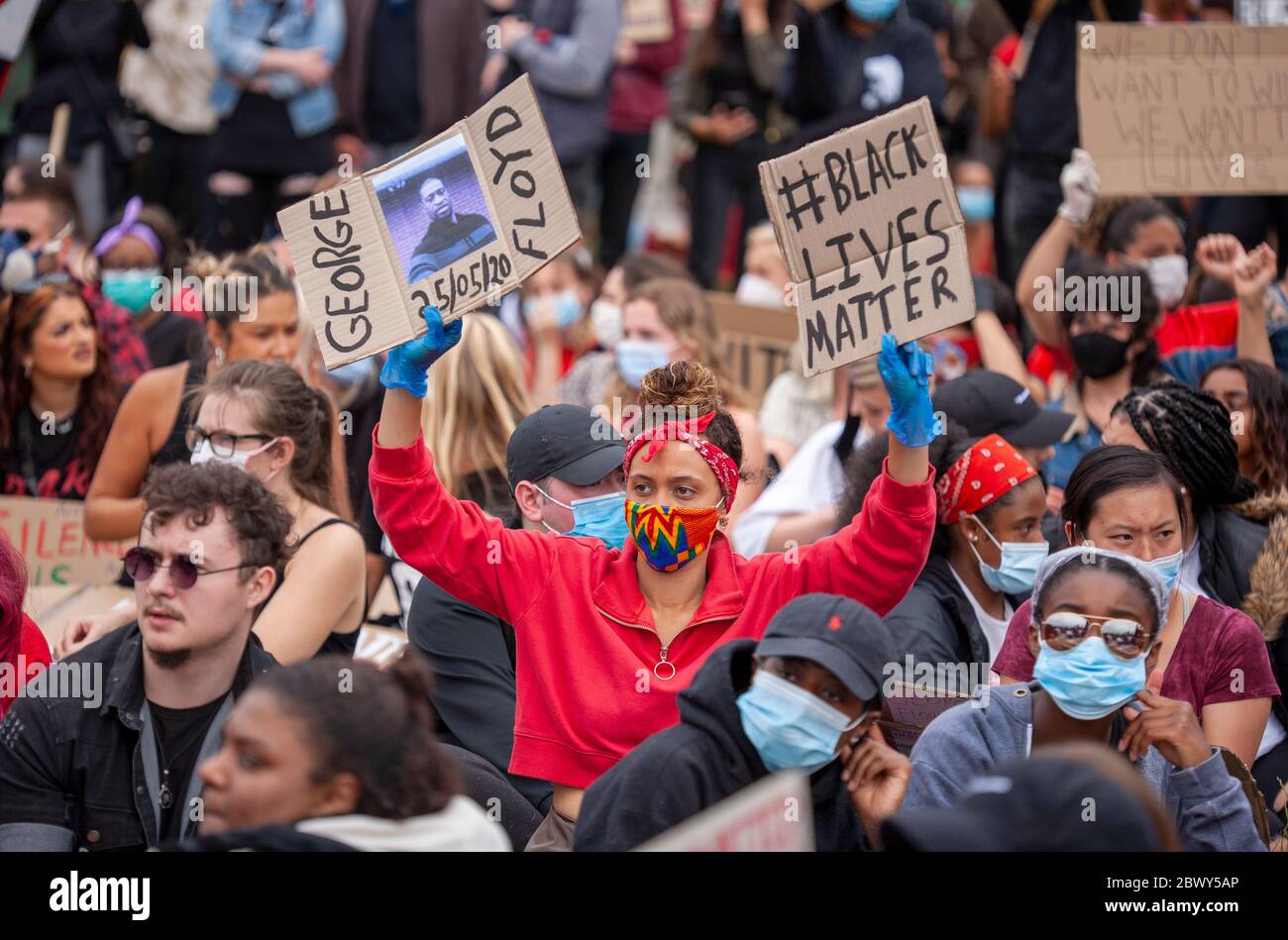 Woman, wearing a face mask and gloves, holding up protest signs during ...