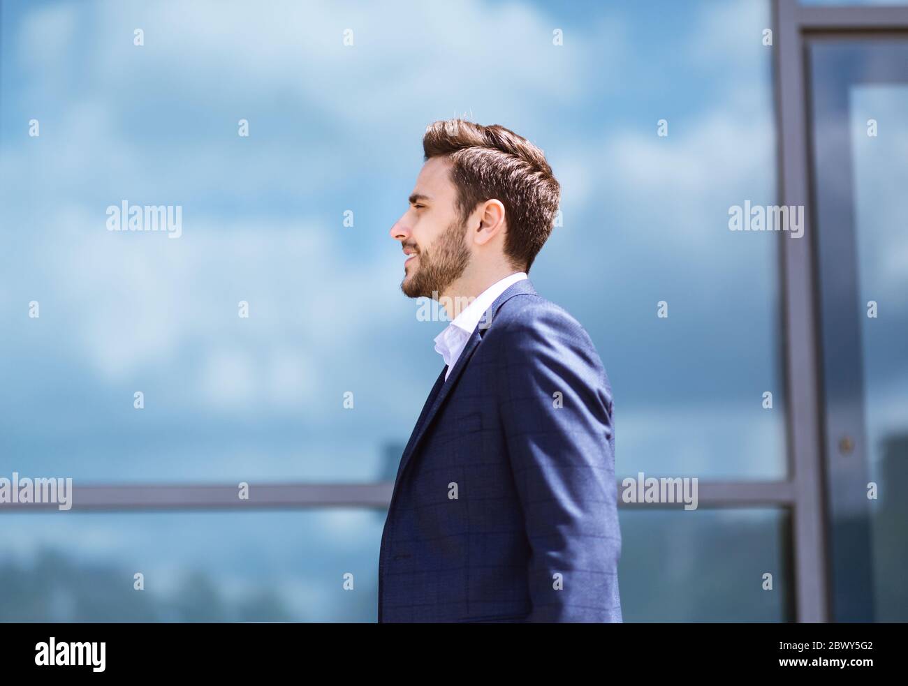 Side view of handsome businessman in front of office building in modern ...