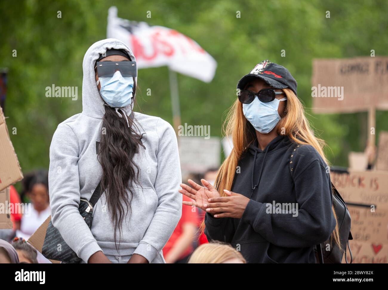 Two women, wearing sunglasses and surgical face masks, stand in Hyde ...