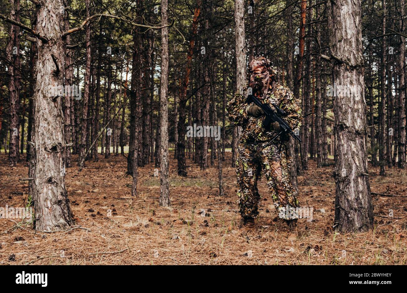 Photo of a camouflaged forest sniper hunter with crossbow standing in ...