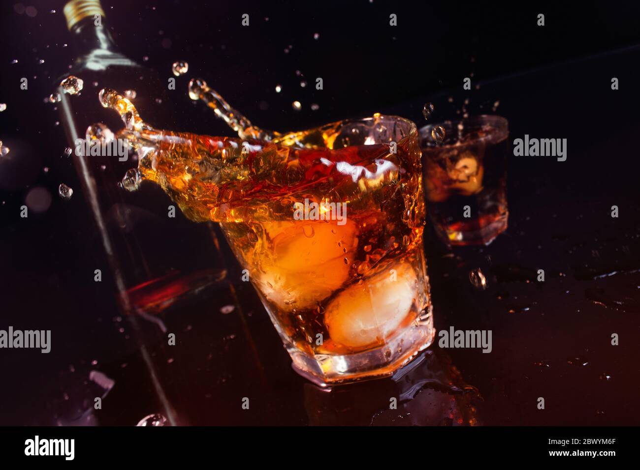 Photo of a whiskey spilling from glasses with ice and bottle on a black ...