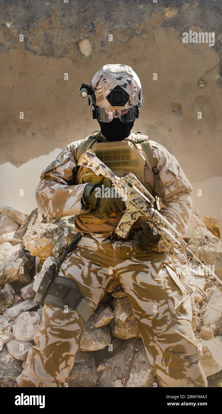 Photo of a fully equipped desert soldier with rifle sitting in stone ...