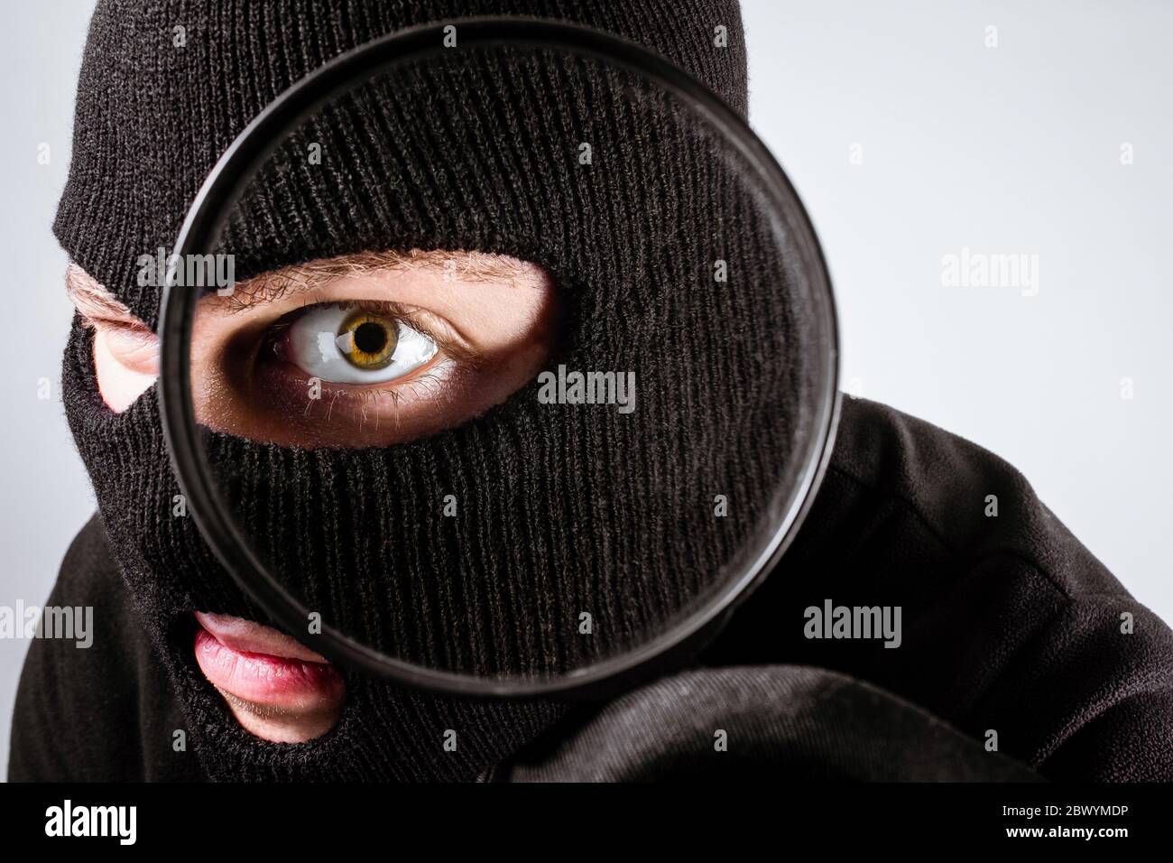 Photo of a male thief in mask looking at magnifying glass on white ...