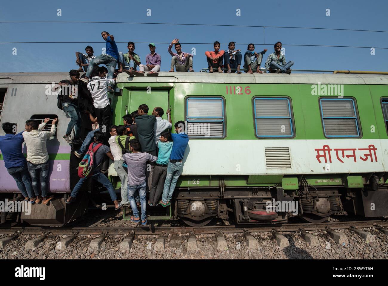 Commuters hang in between rail cars and sit on the roof of an ...
