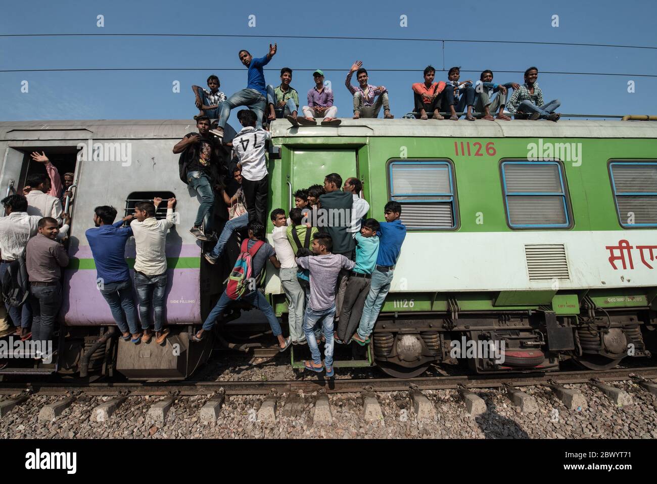 Commuters hang in between rail cars and sit on the roof of an ...