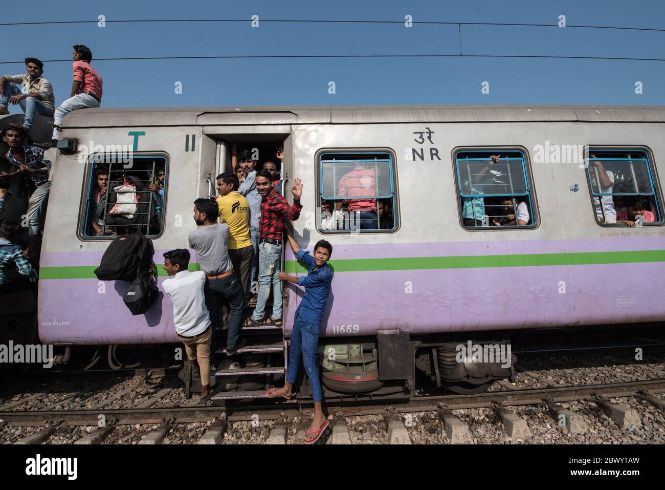Commuters hang in between rail cars and sit on the roof of an ...