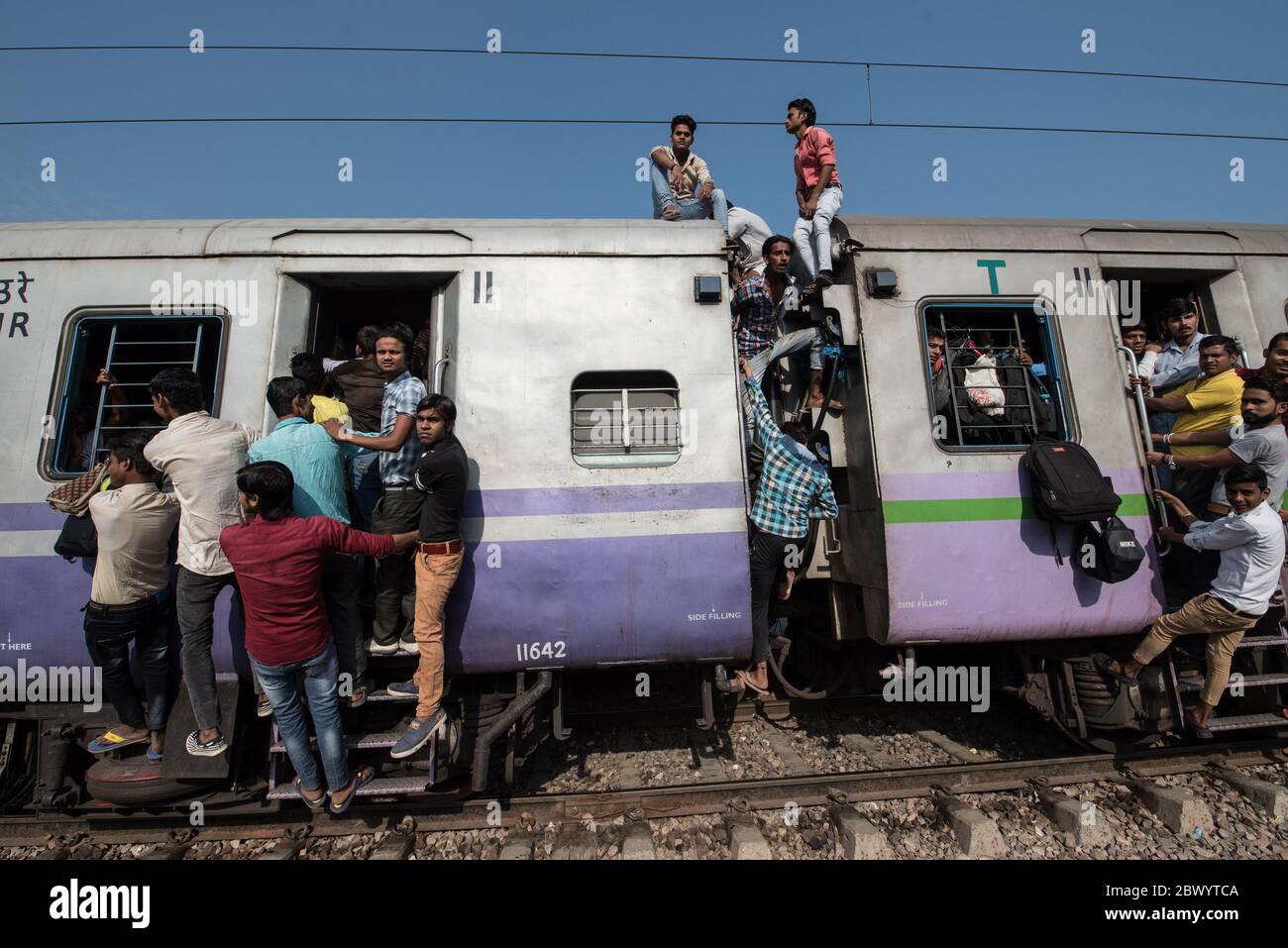 Commuters hang in between rail cars and sit on the roof of an ...