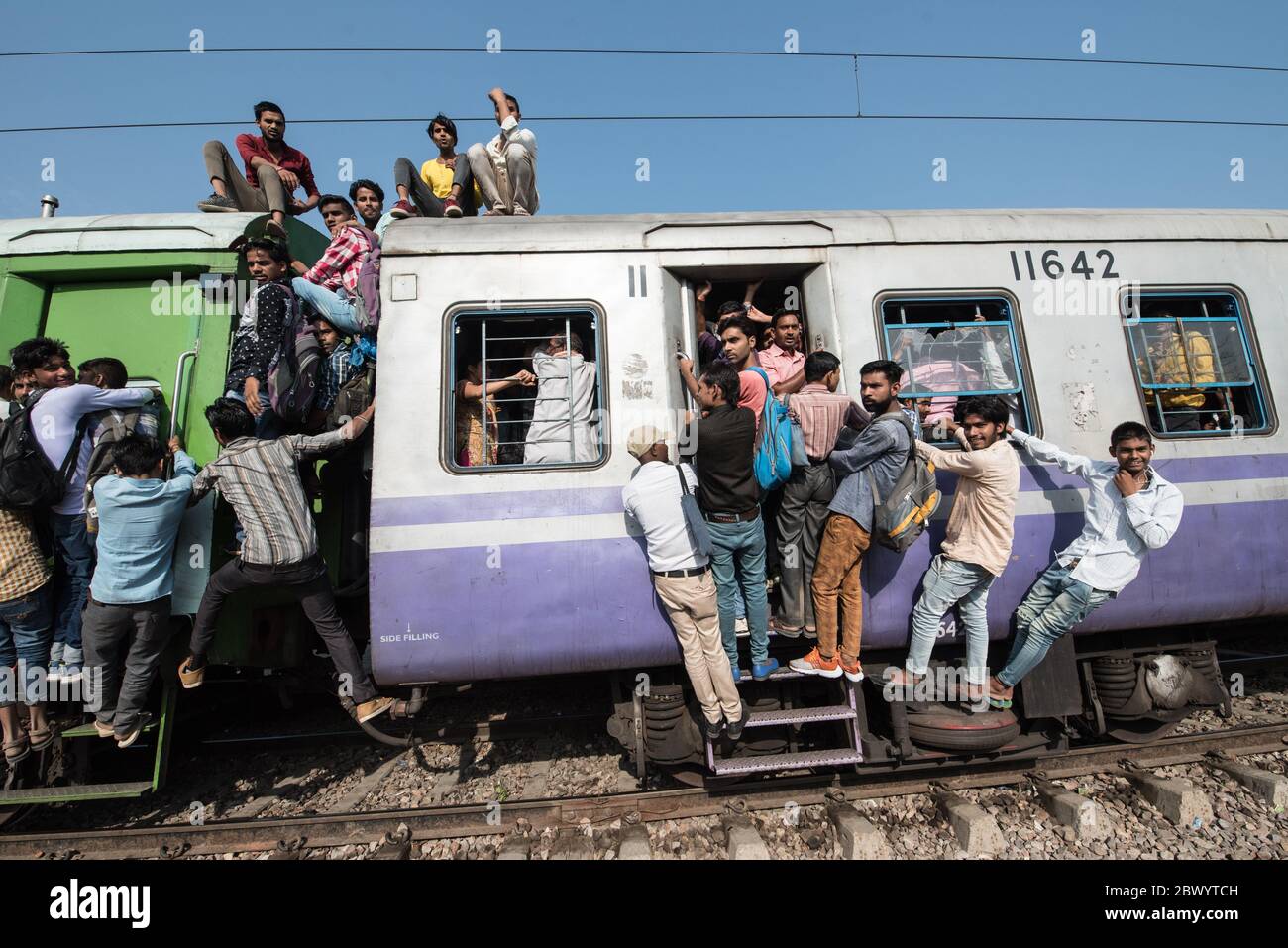 Commuters hang in between rail cars and sit on the roof of an ...