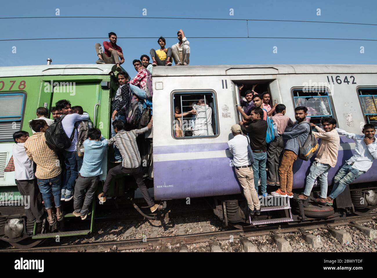 Commuters hang in between rail cars and sit on the roof of an ...