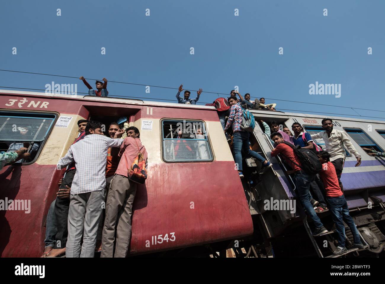Commuters hang in between rail cars and sit on the roof of an ...