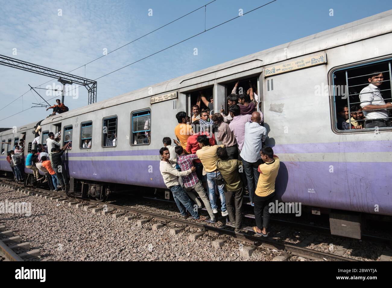 Commuters hang out of an overcrowded Indian Railways train, at Noli ...