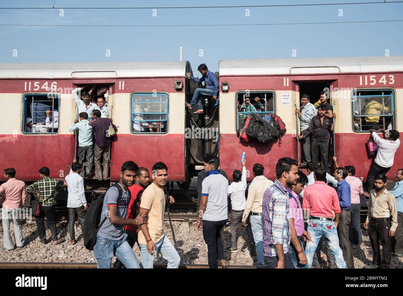 Commuters hang in between rail cars and sit on the roof of an ...