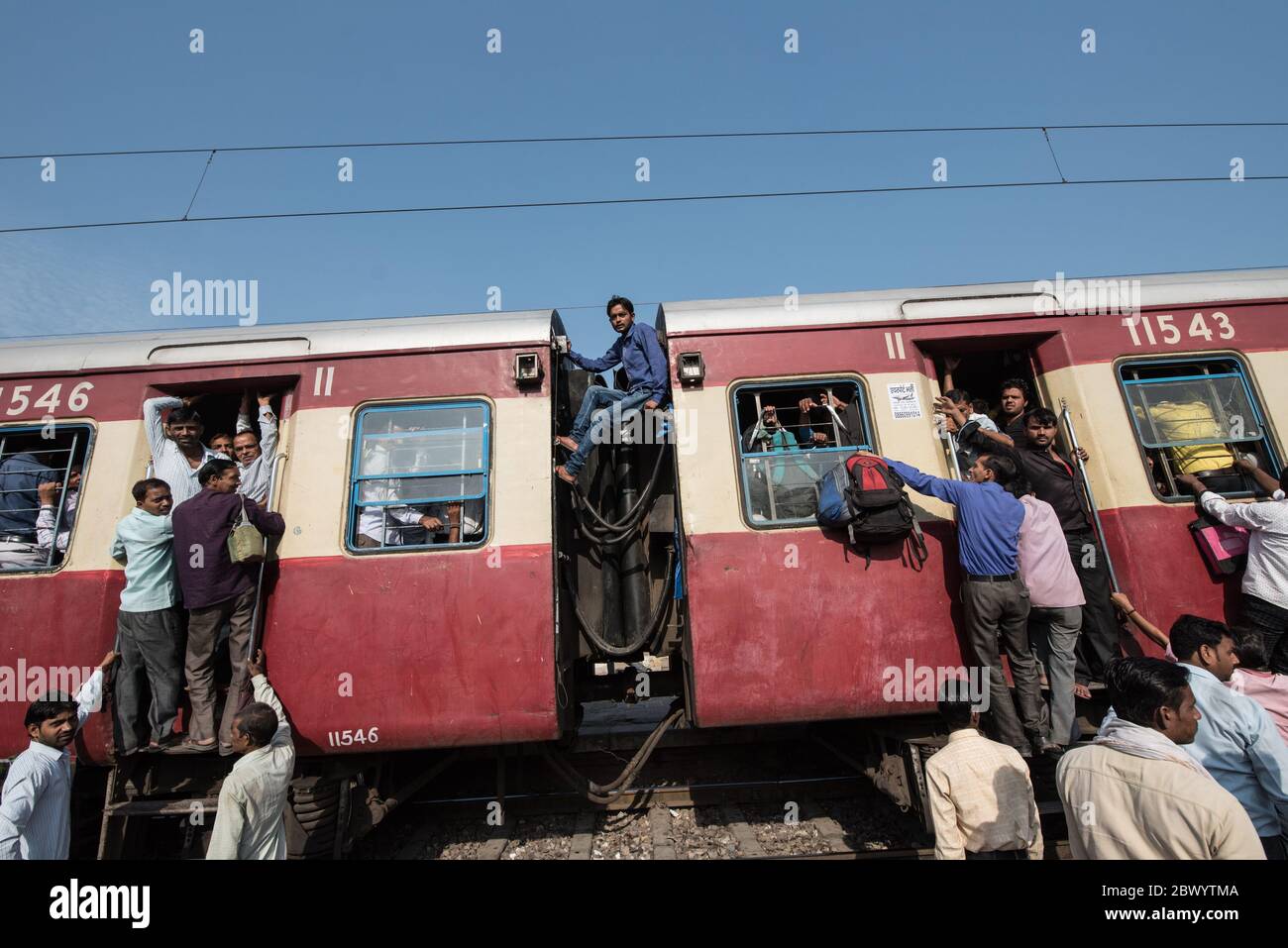 Commuters hang in between rail cars and sit on the roof of an ...
