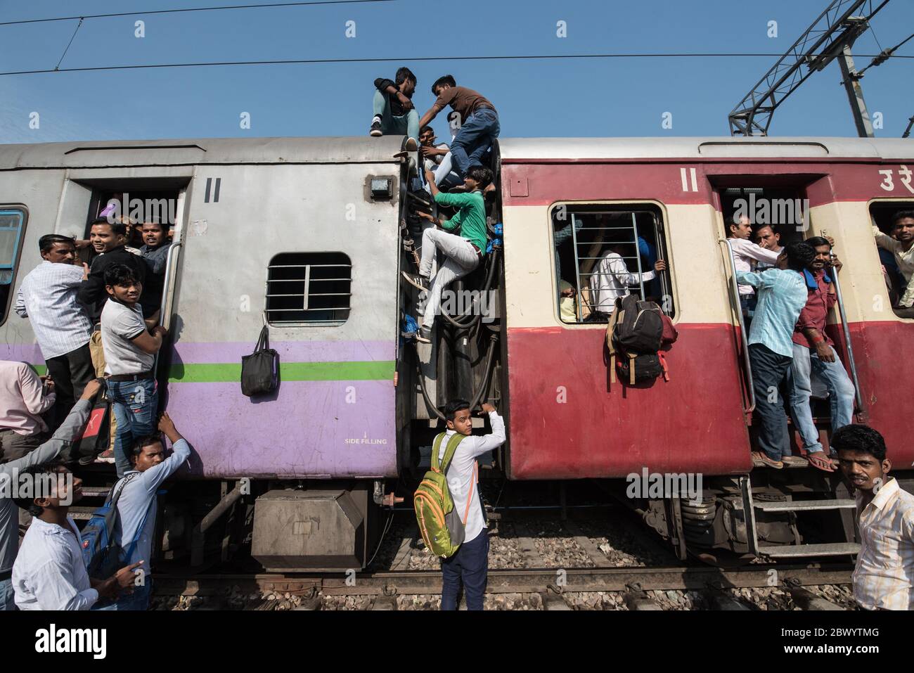 Commuters hang in between rail cars and sit on the roof of an ...