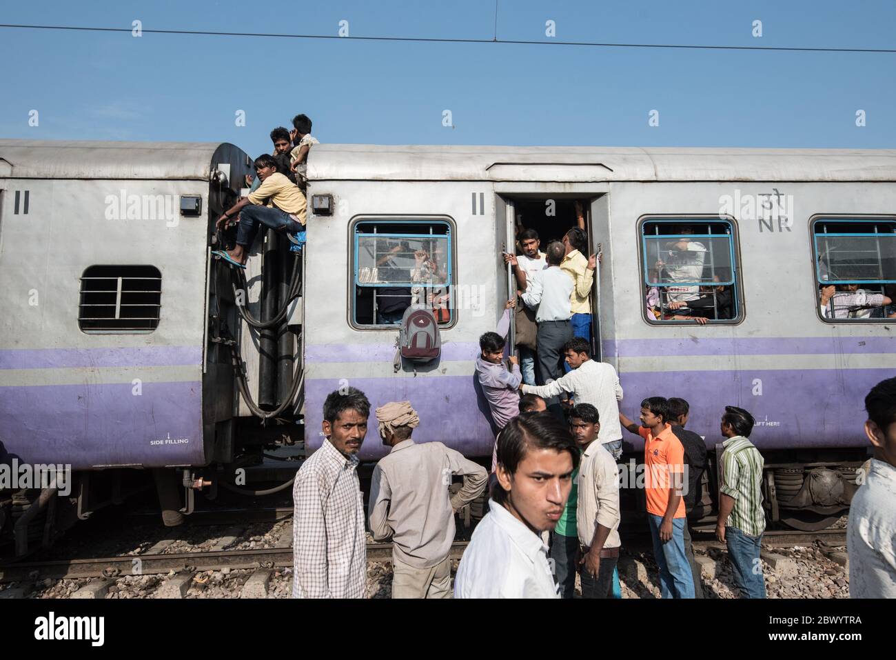 Commuters hang in between rail cars and sit on the roof of an ...