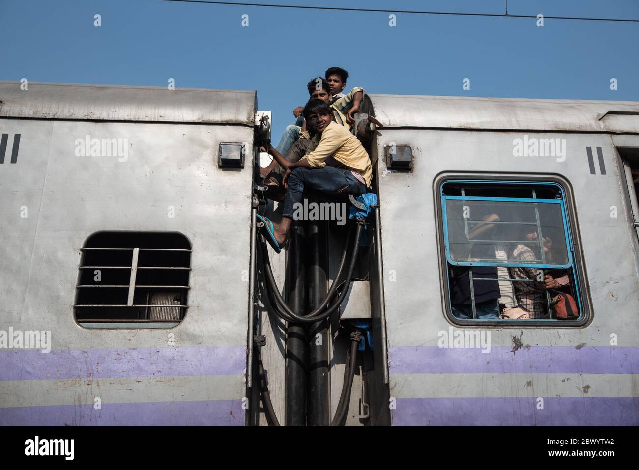 Commuters hang in between rail cars and sit on the roof of an ...