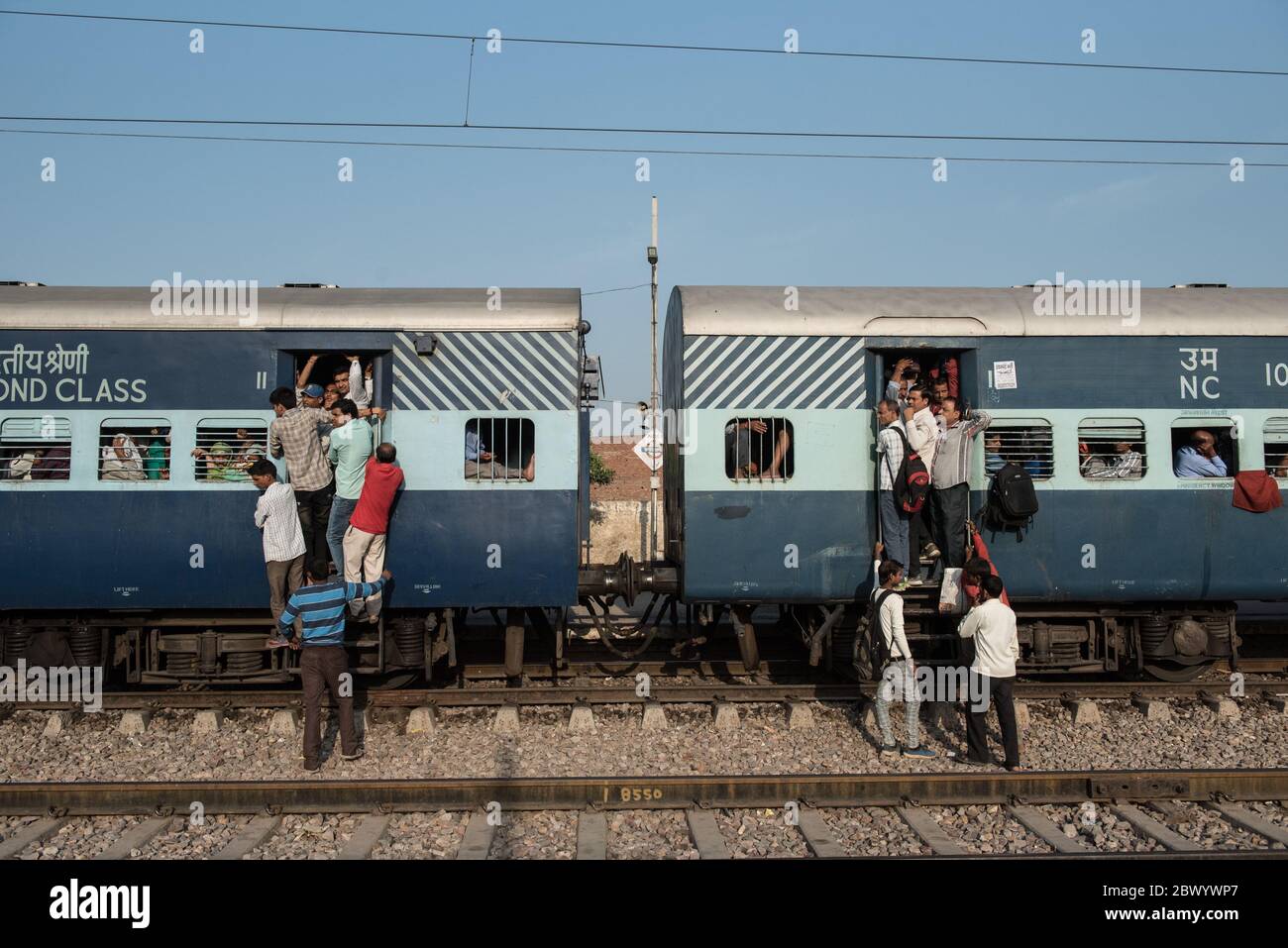 Commuters hang out of an overcrowded Indian Railways train, at Noli ...