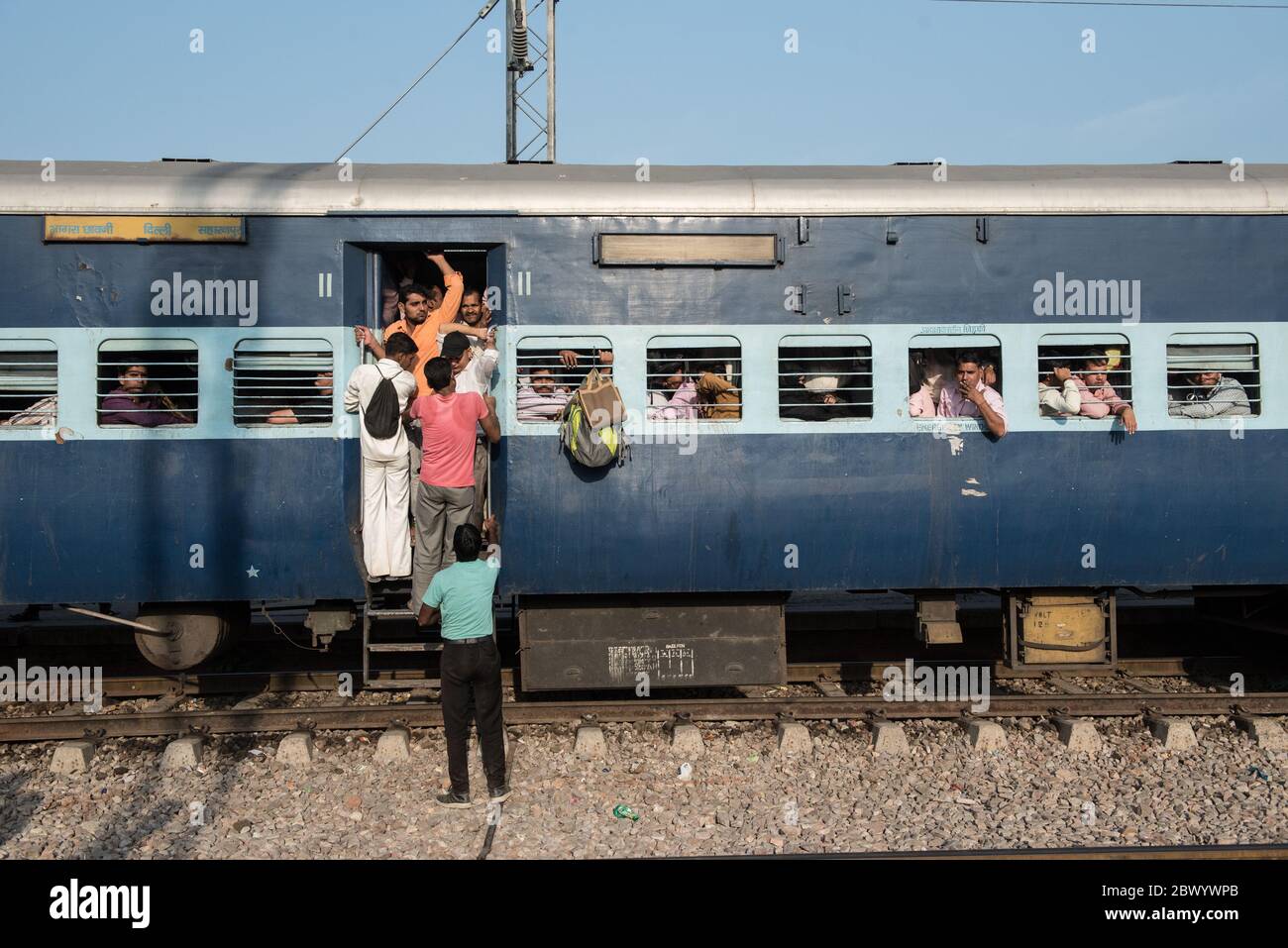 Commuters hang out of an overcrowded Indian Railways train, at Noli ...