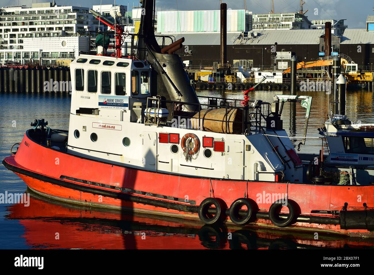 Steel tug boat with red hull and white cabin on calm surface of port ...