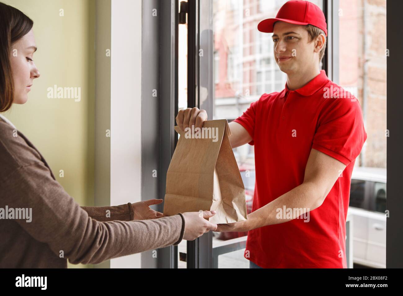 Fast food delivery. Girl receives paper bag with order from courier ...