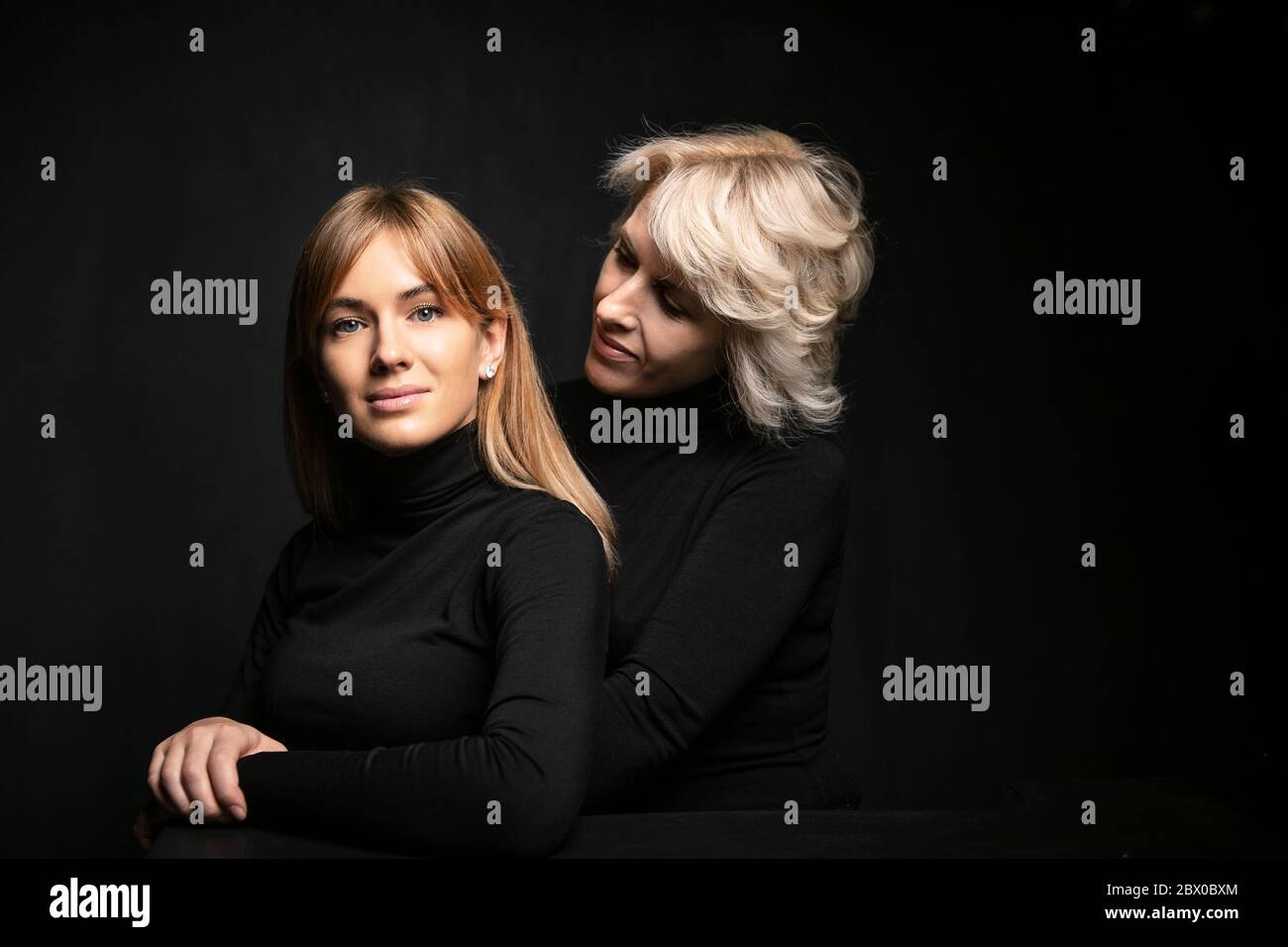 Mom looks at her daughter. tender family photo. studio models on black ...