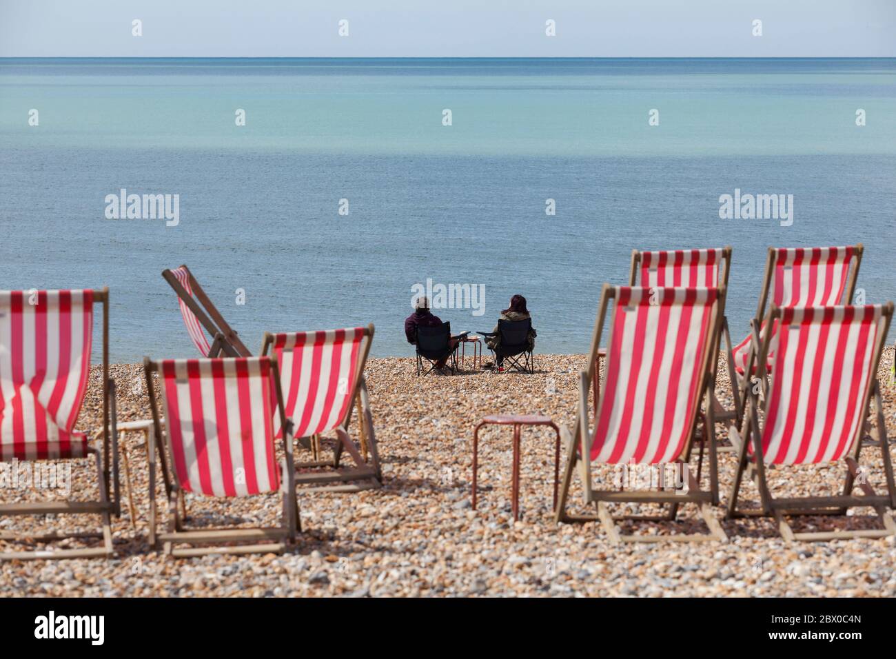 Horizontal view to folding beach chairs and two sitting people on the ...