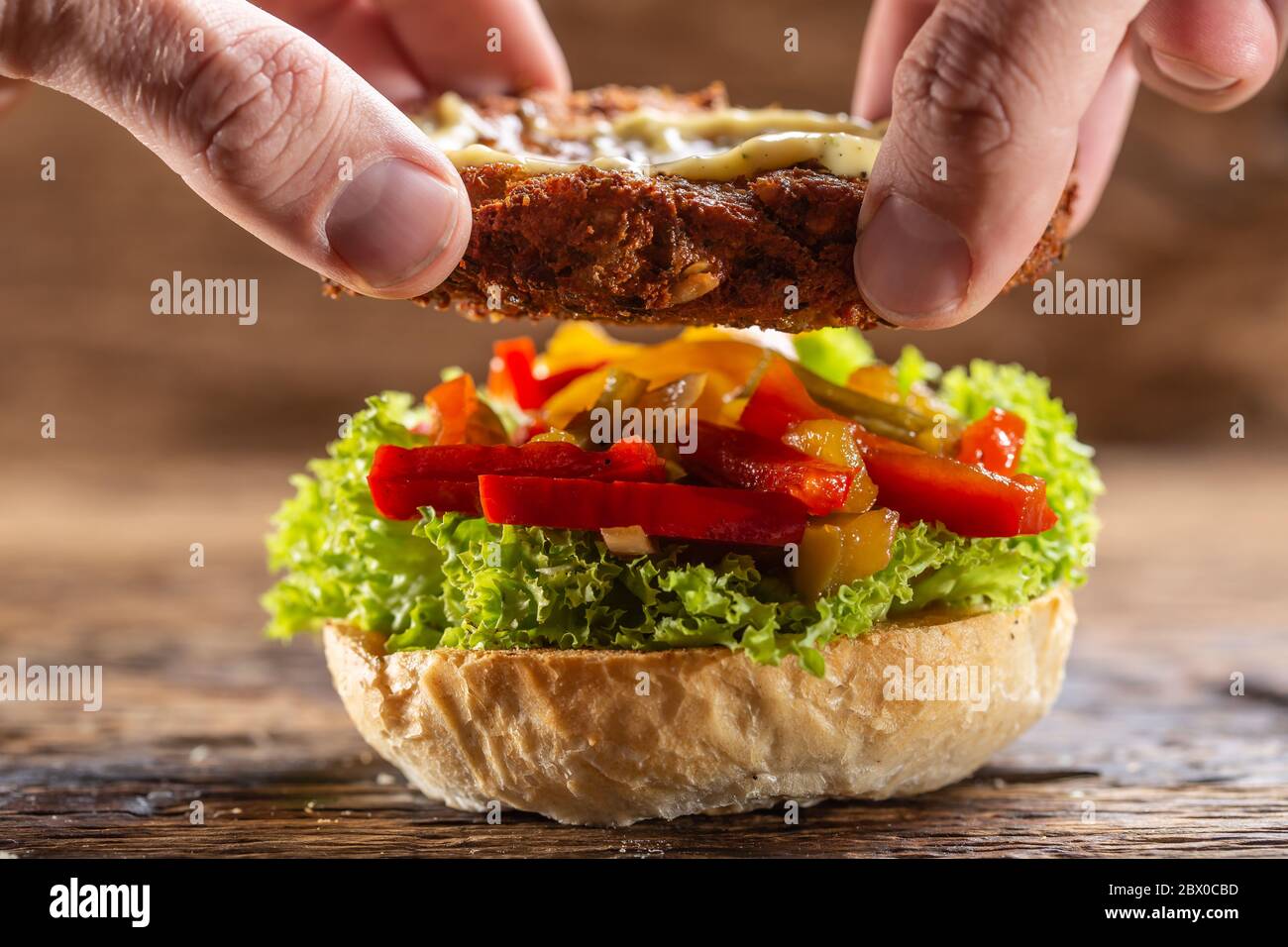 Composing a burger, placing the meat part onto layers of salad and ...