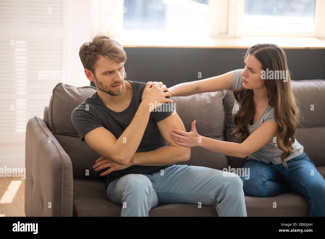 Long-haired young woman blaming her husband while he sitting with upset ...