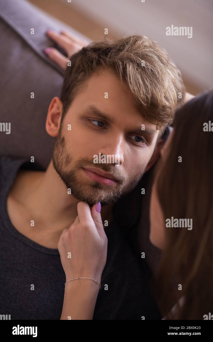 Young bearded man looking serious while his wife touching his face ...