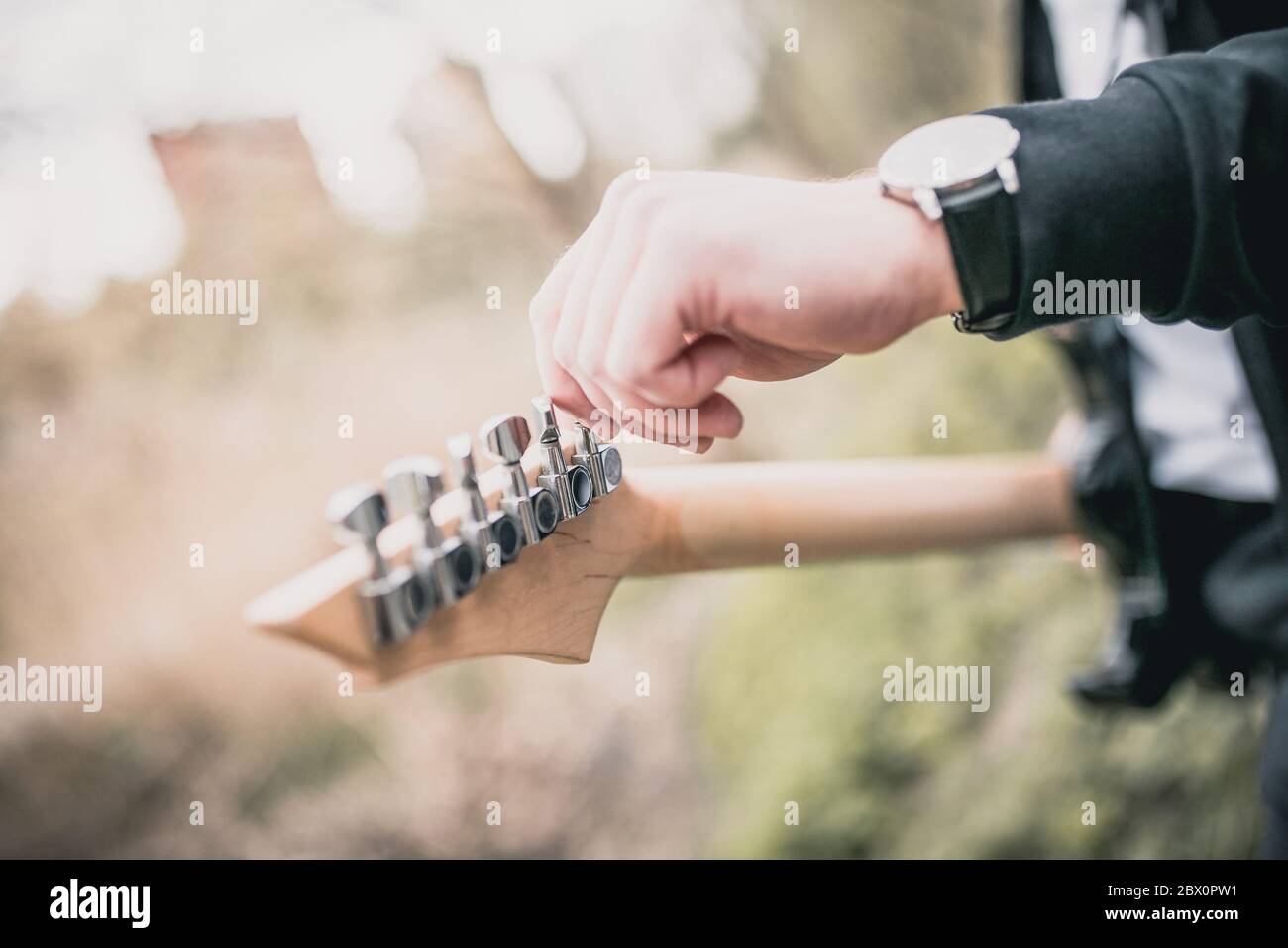A man tunes a black electric guitar in the open air - twists the ...