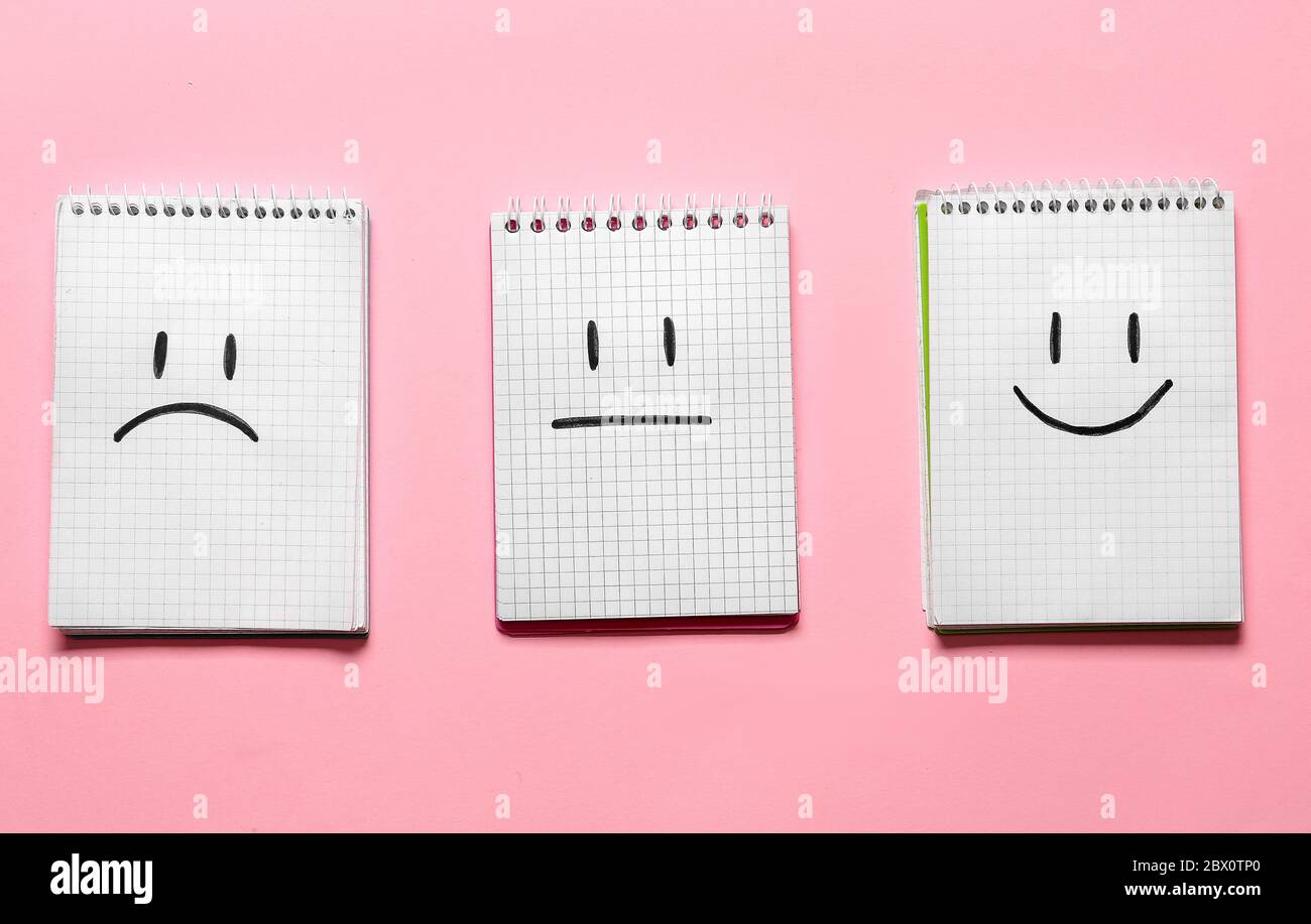 Notebooks with drawn sad, happy and neutral faces on color background ...
