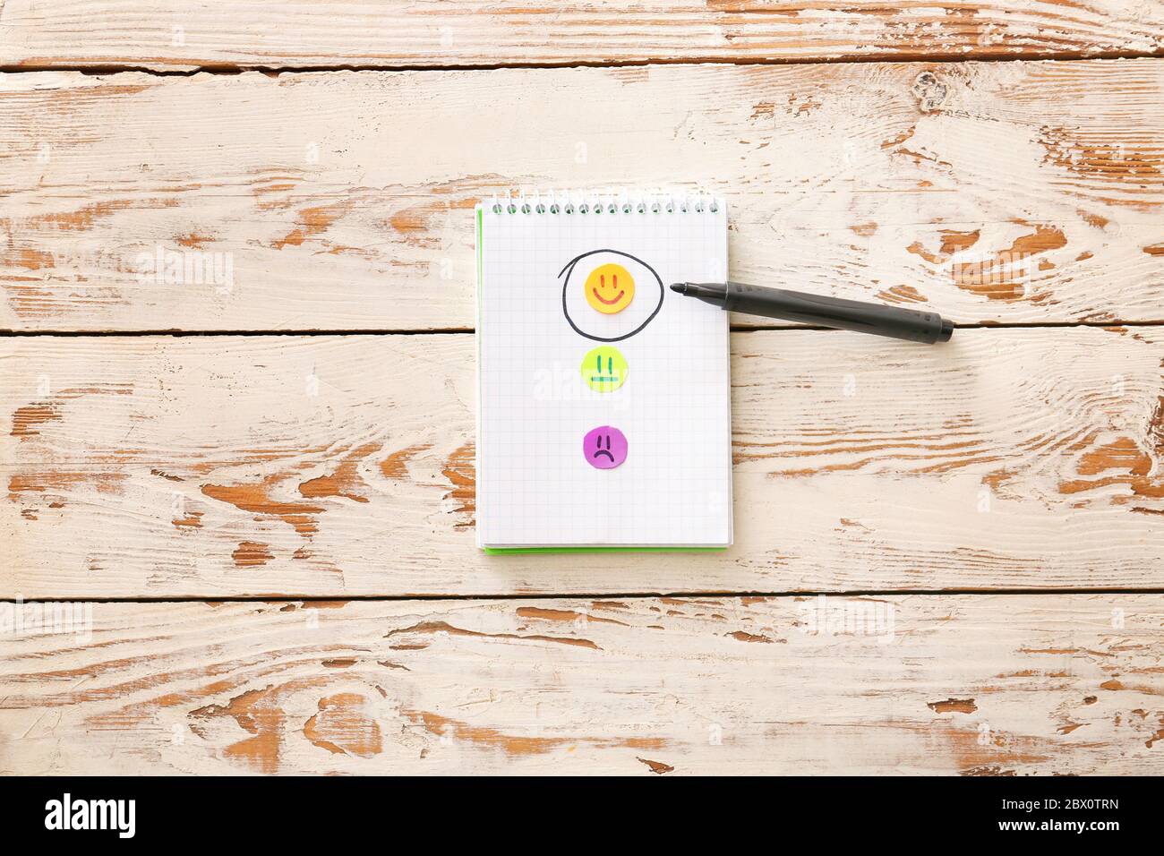 Notebook with drawn sad, happy and neutral faces on white wooden ...