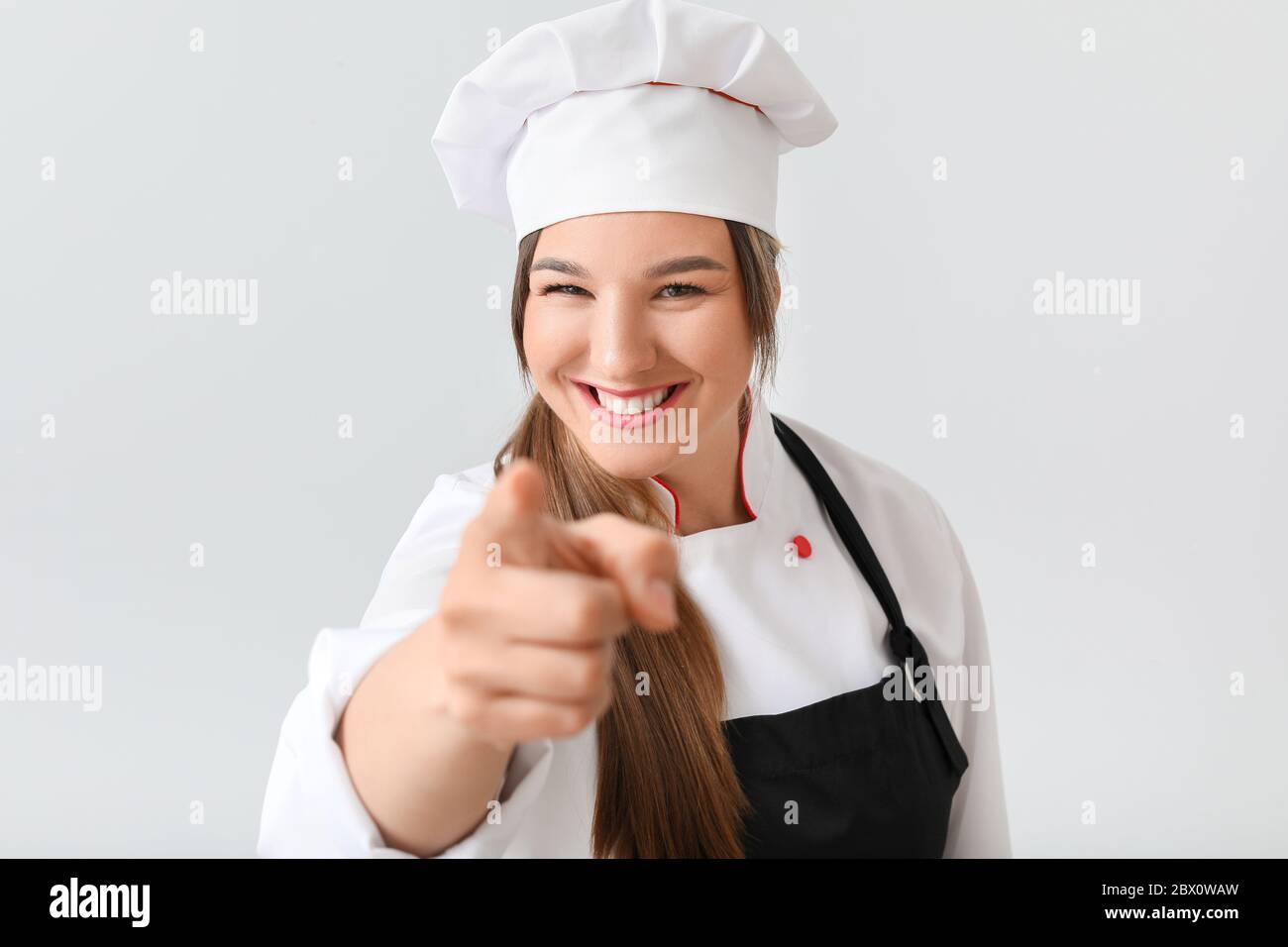 Young female chef pointing at viewer on light background Stock Photo ...